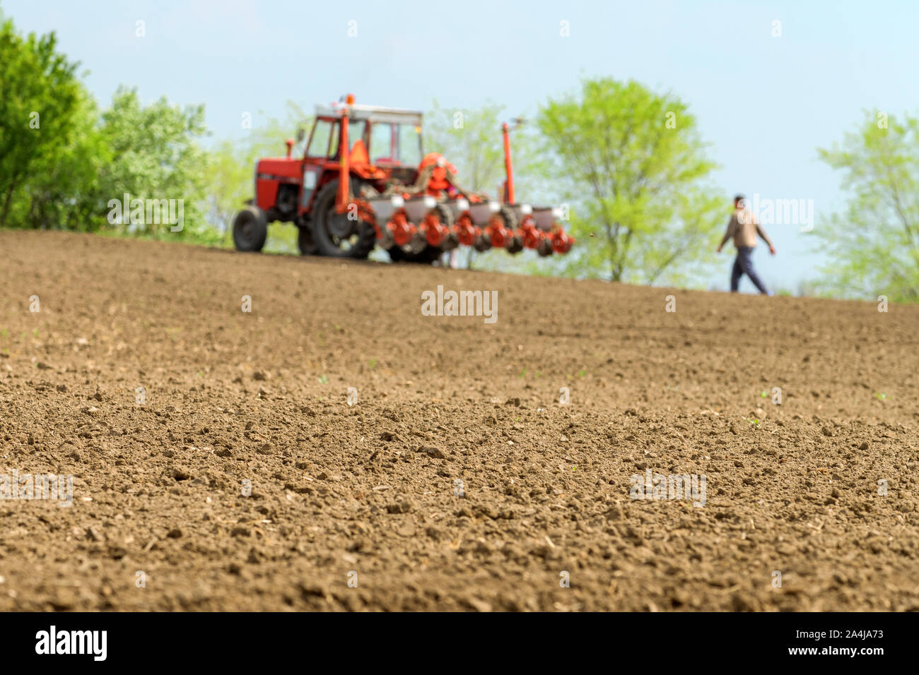 Farmer repairing tractor with seeder in field during corn crop planting ...