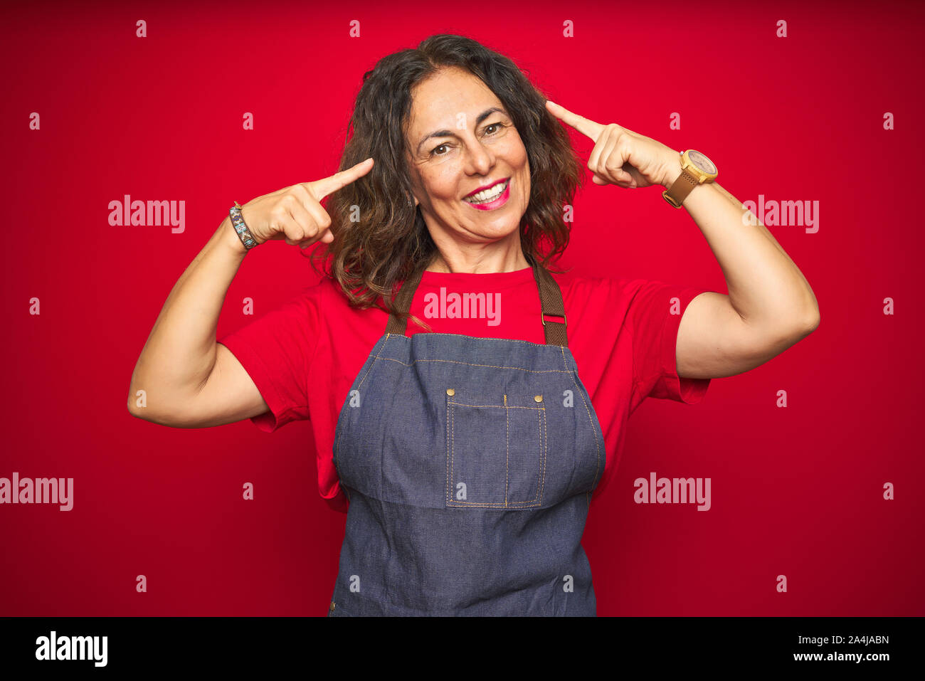 Middle age senior woman wearing apron uniform over red isolated ...