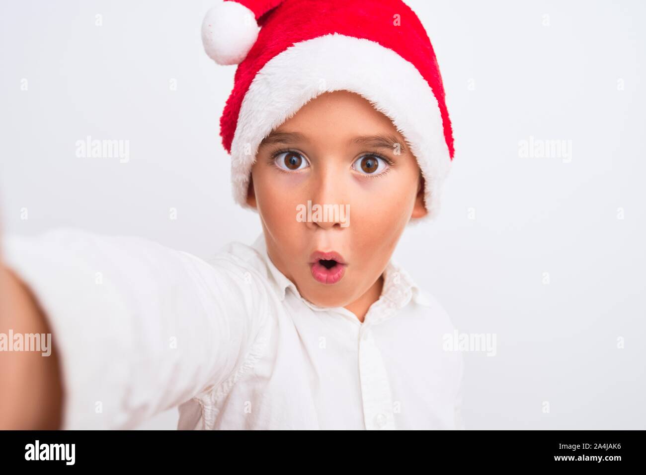 Beautiful kid boy wearing Christmas Santa hat make selfie over isolated ...