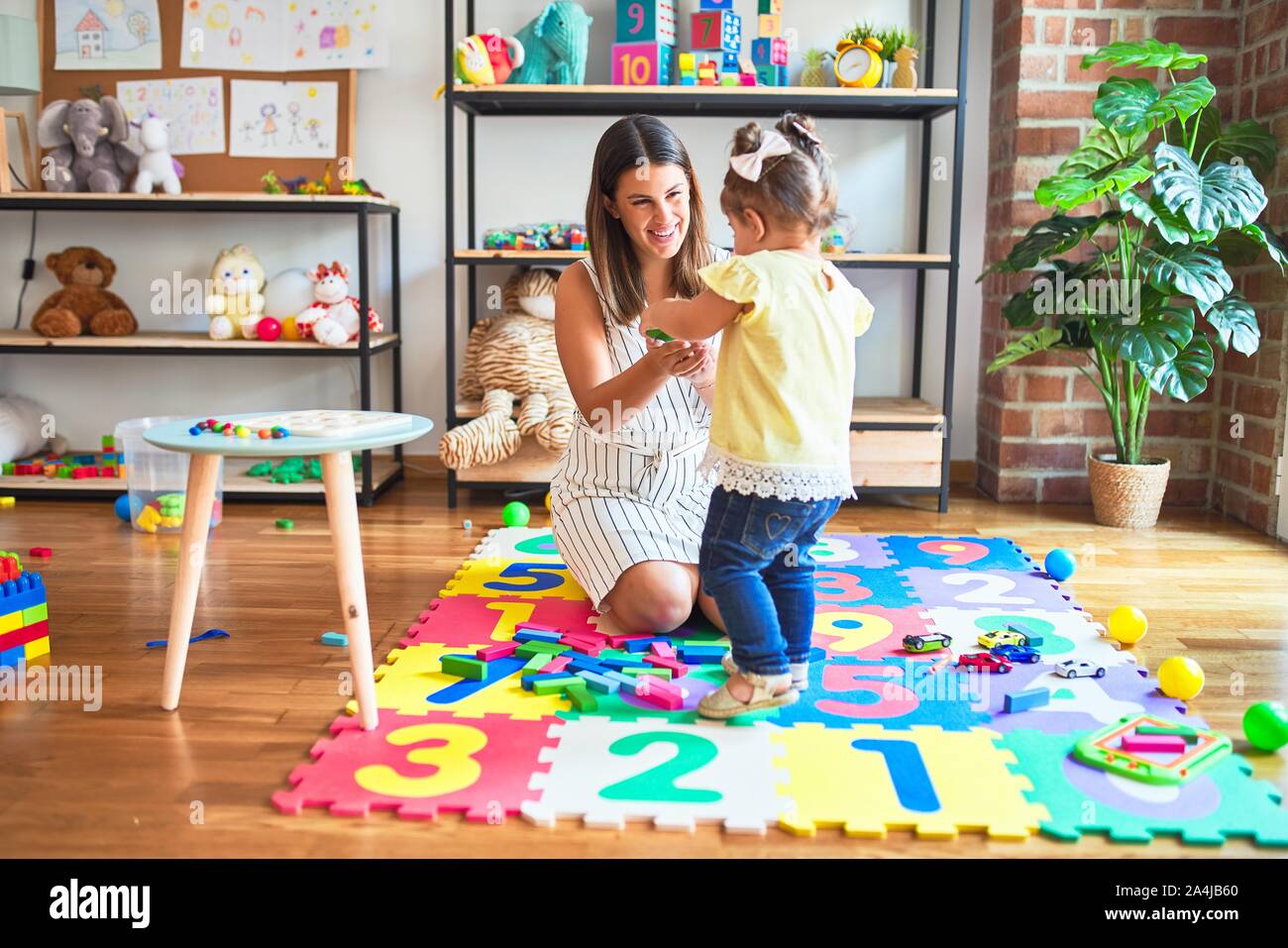 Young beautiful teacher and toddler playing with building wooden blocks ...