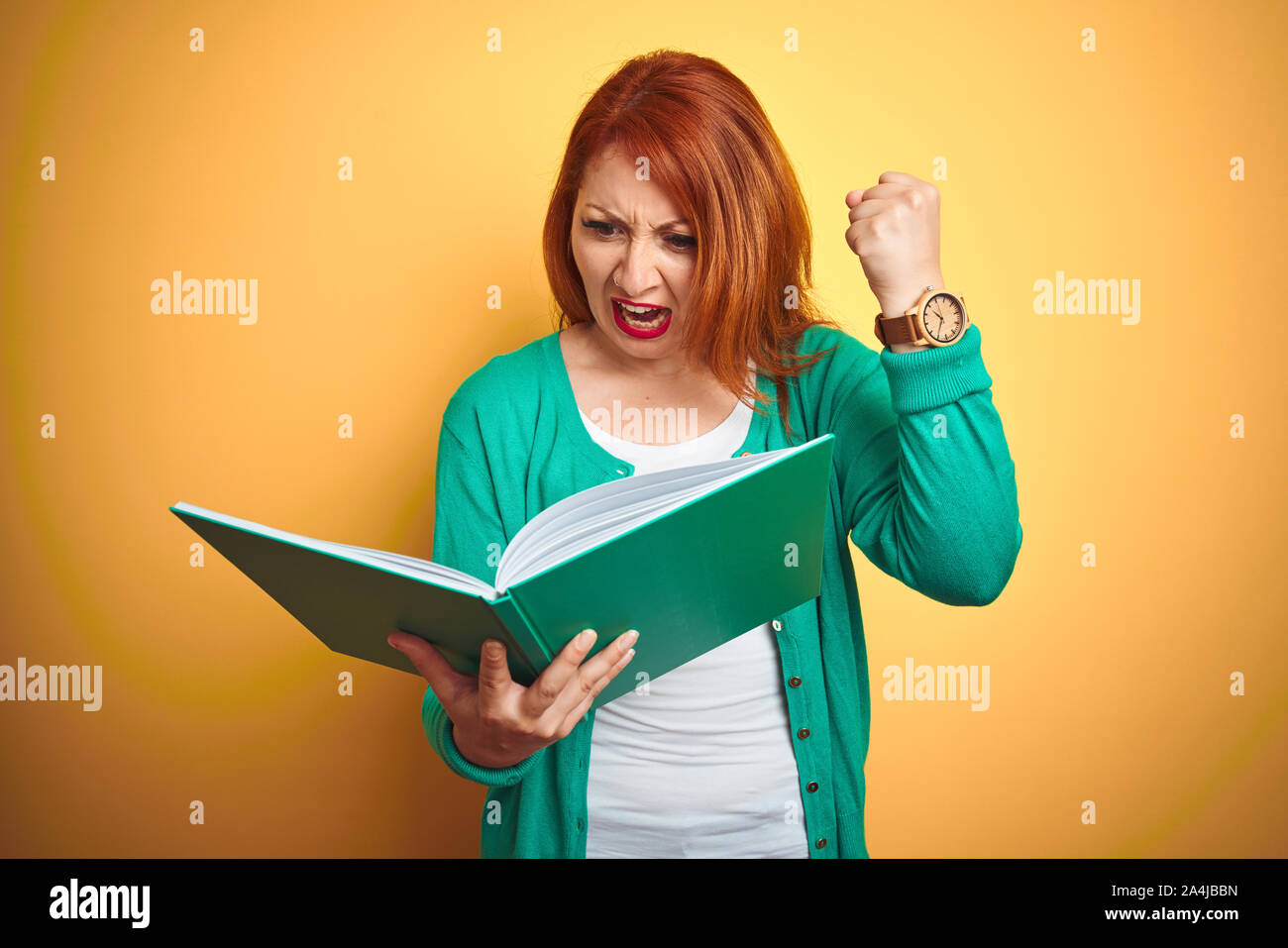 Young redhead student woman reading green book over yellow isolated ...