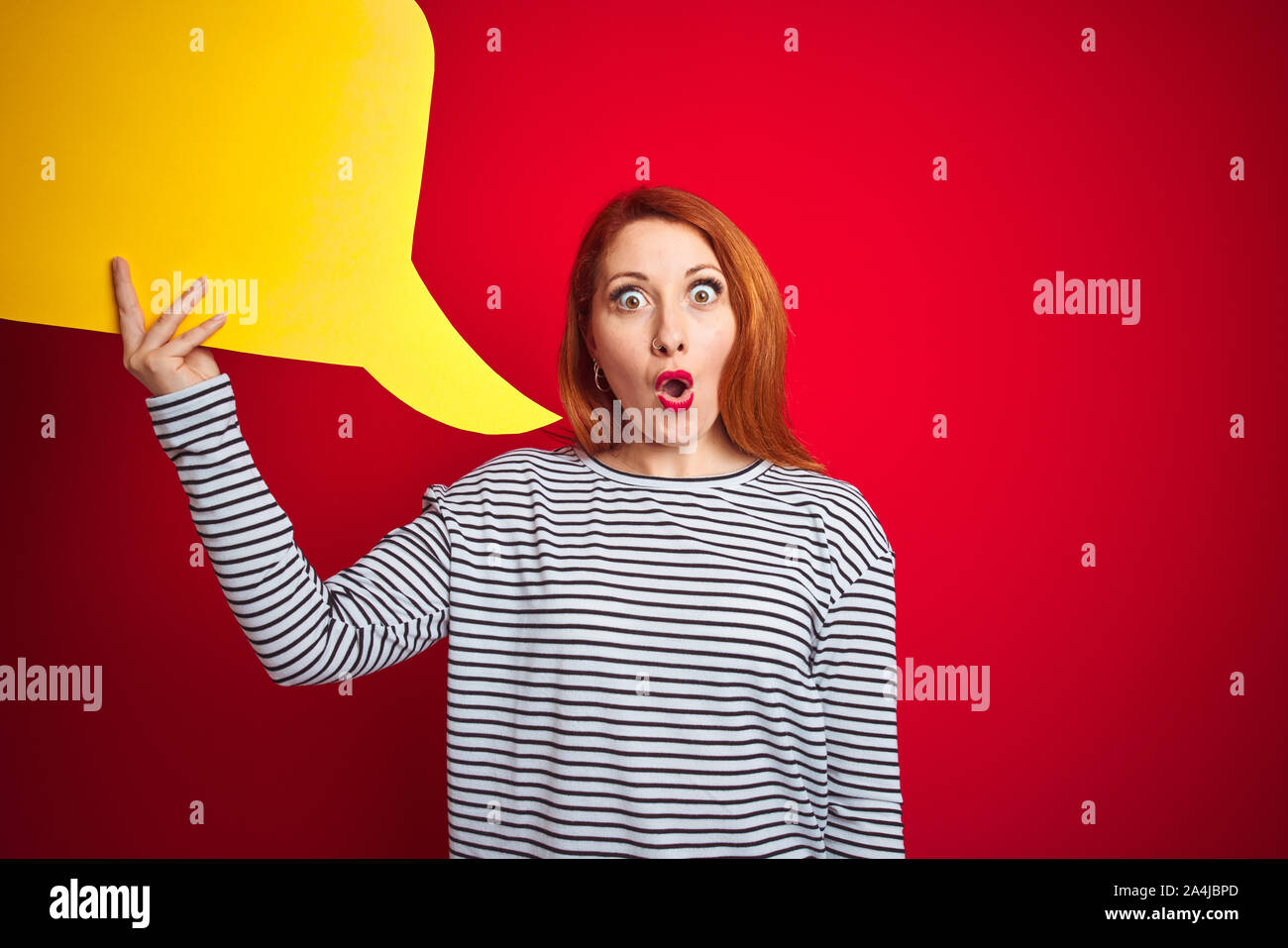 Young beautiful redhead woman holding yellow speech bubble over red ...