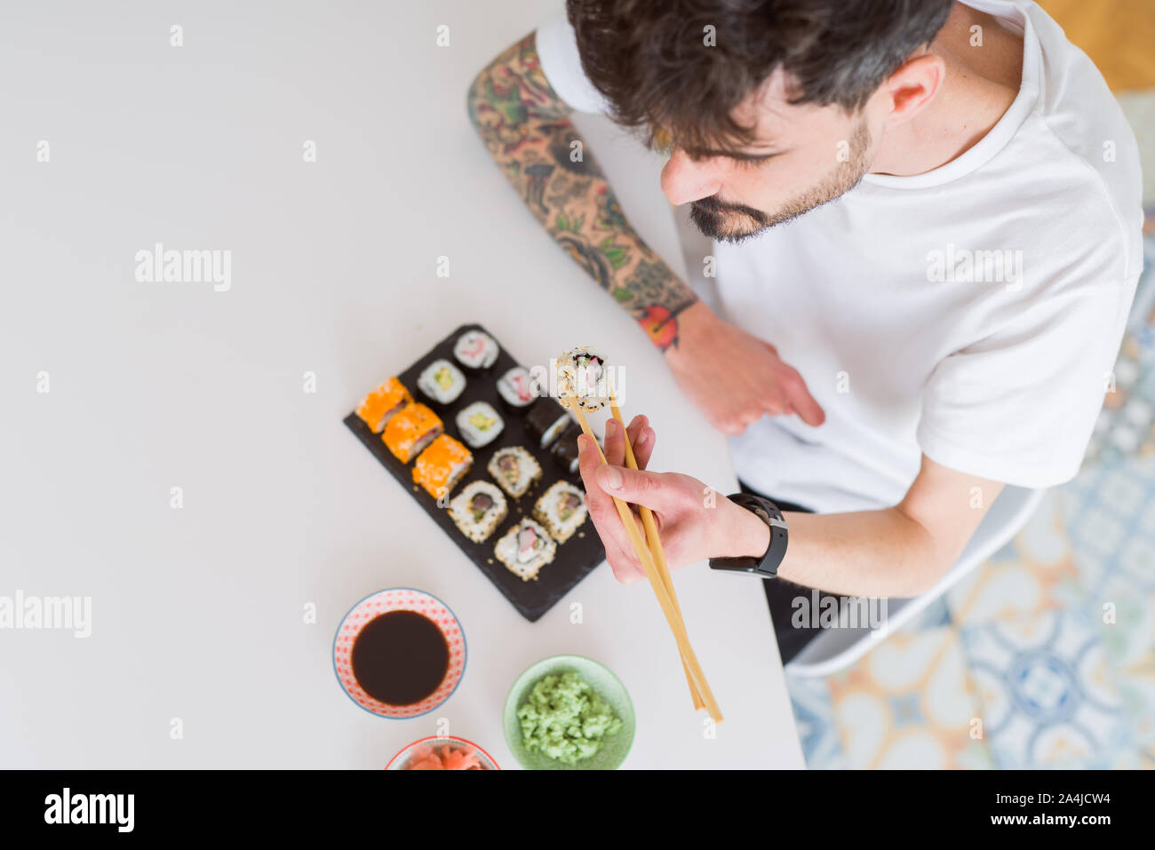 Overhead angle of young man eating sushi asian food using choopsticks ...
