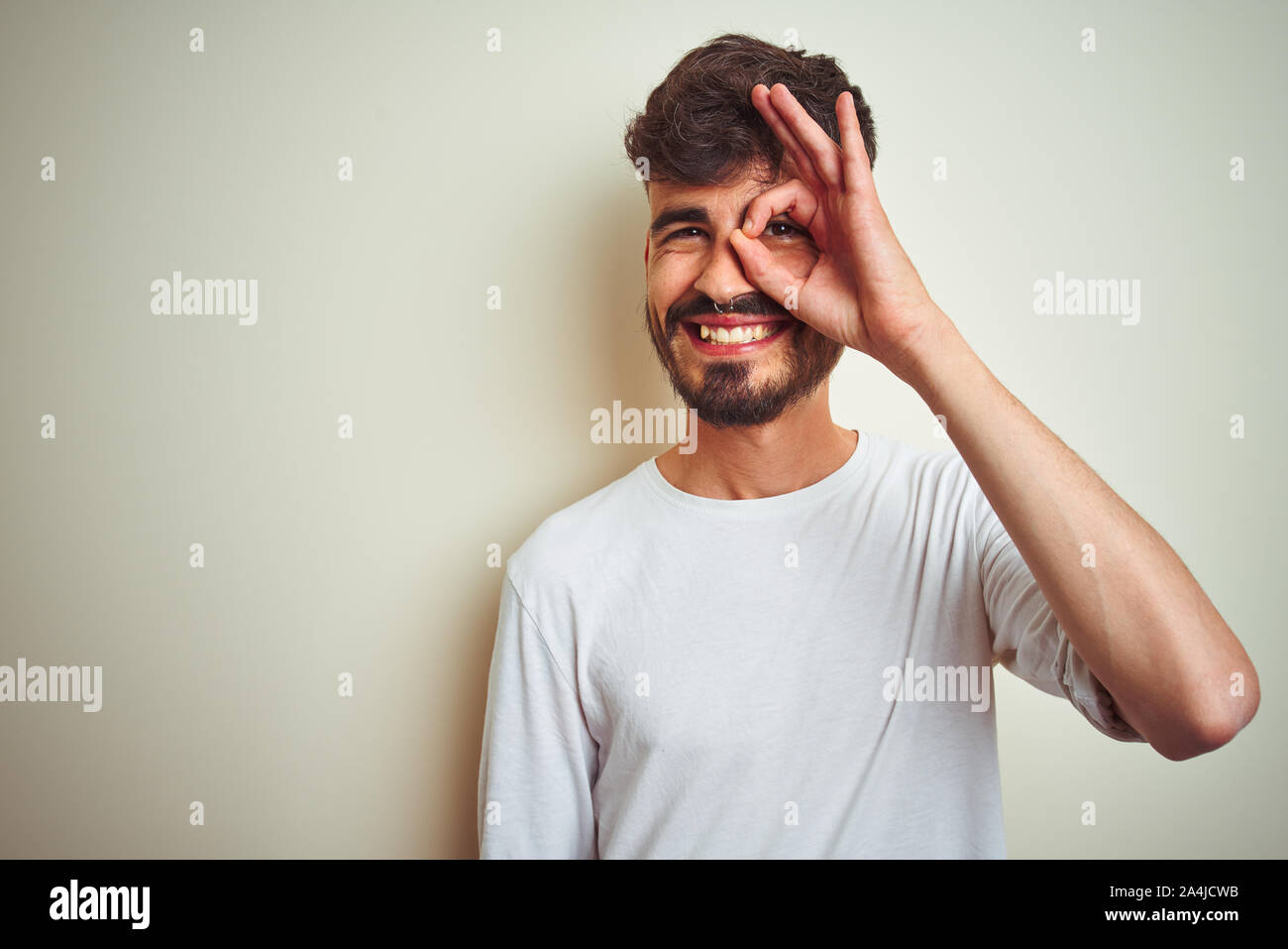 Young man with tattoo wearing t-shirt standing over isolated white background doing ok gesture ...