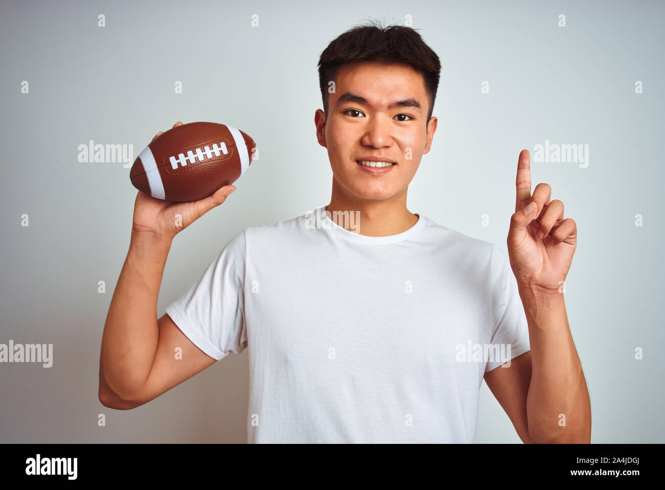 Young asian chinese sportsman holding rugby ball standing over isolated ...
