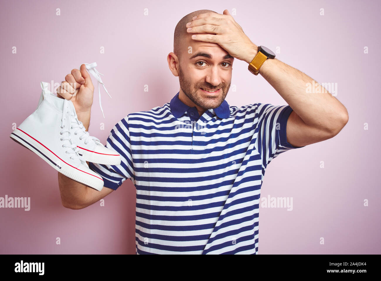 Young man holding casual sneakers shoes over pink isolated background ...