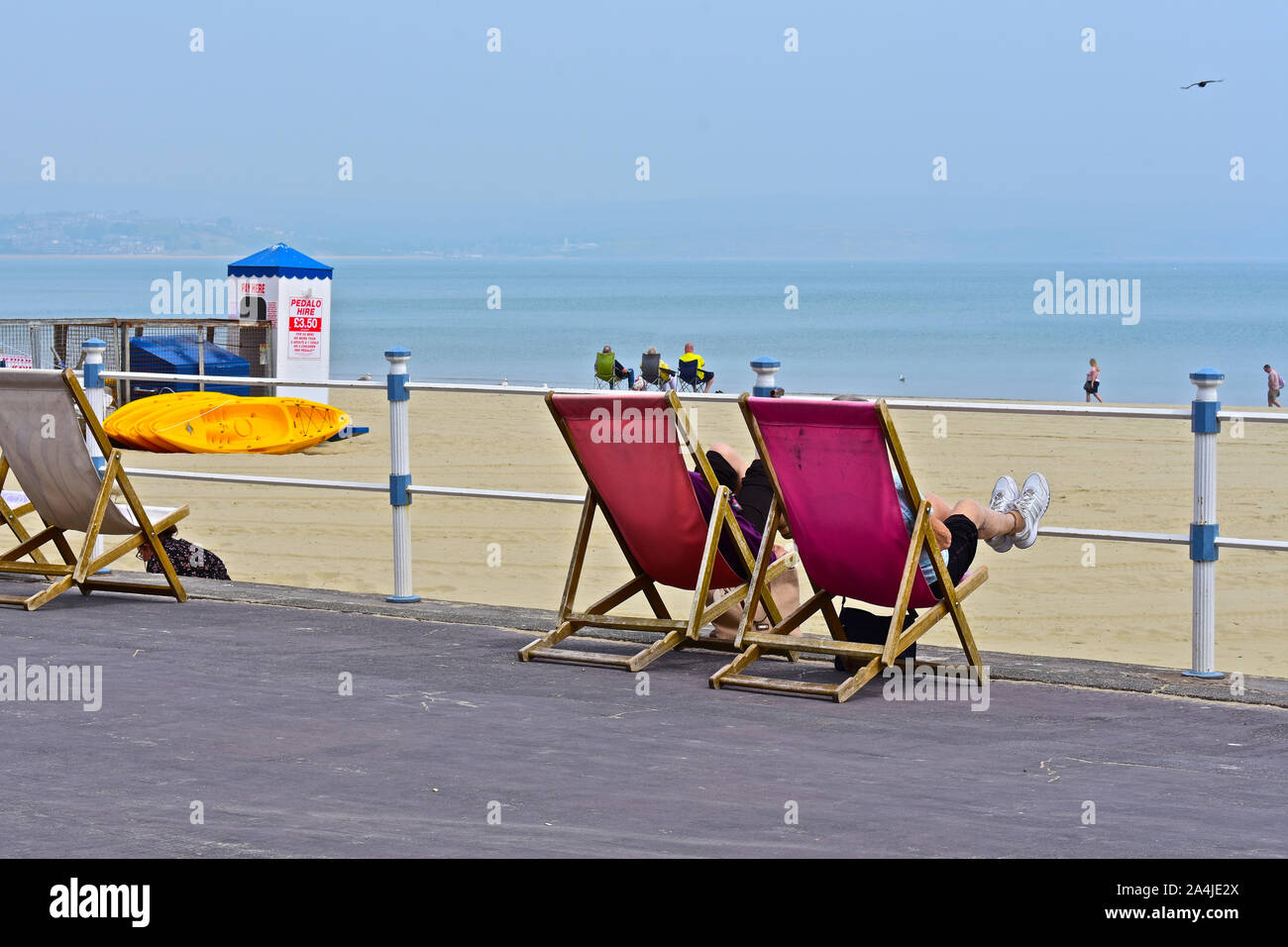 Traditional English seaside scene with people sitting in deck chairs on ...