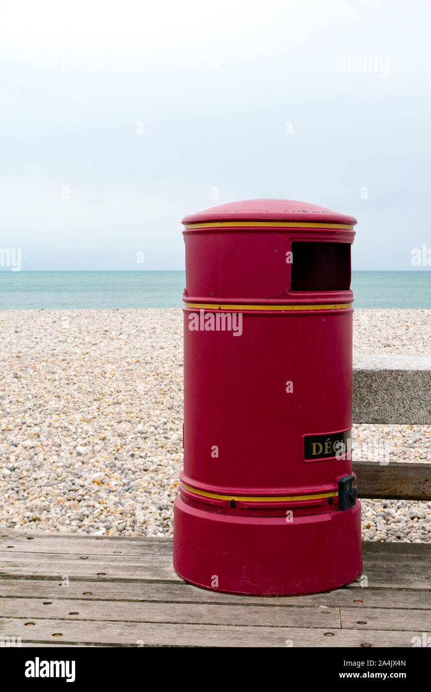 A large vintage red trash can on a wooden boardwalk at a rocky beach ...