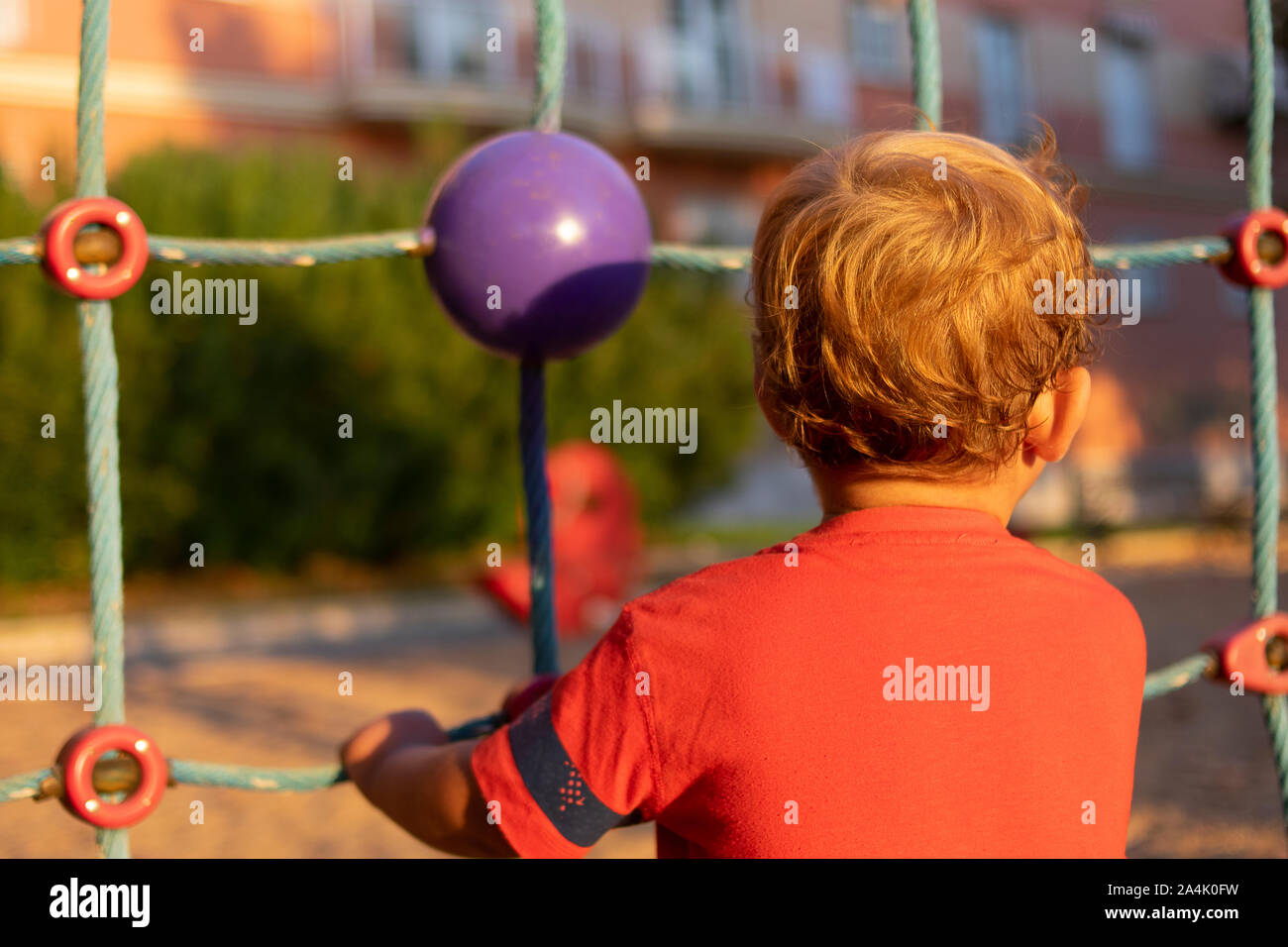 little boy climbing through a net of a children's playground at sunset ...