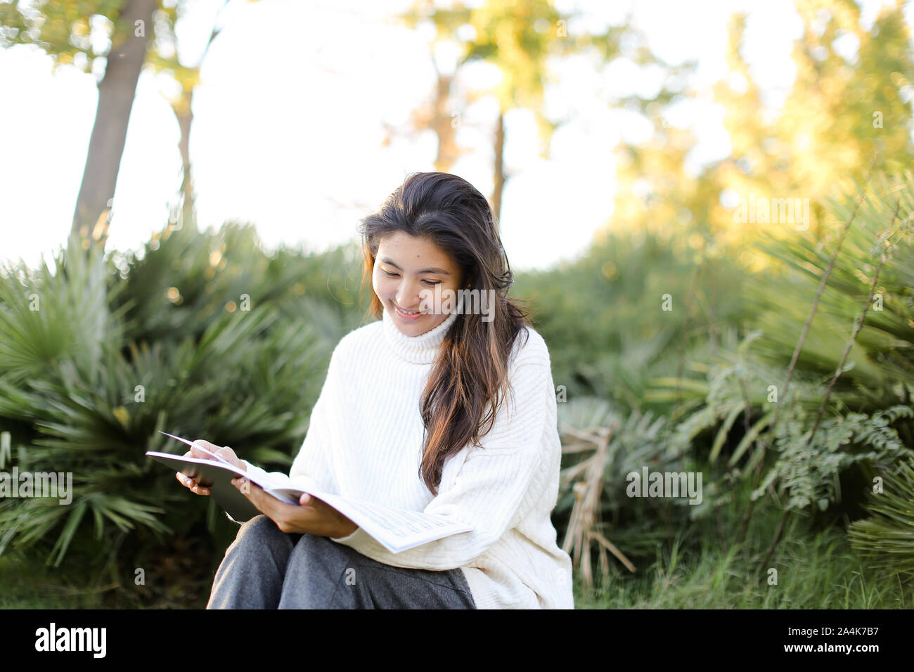 Chinese happy girl sitting on stump in park and reading papers Stock ...