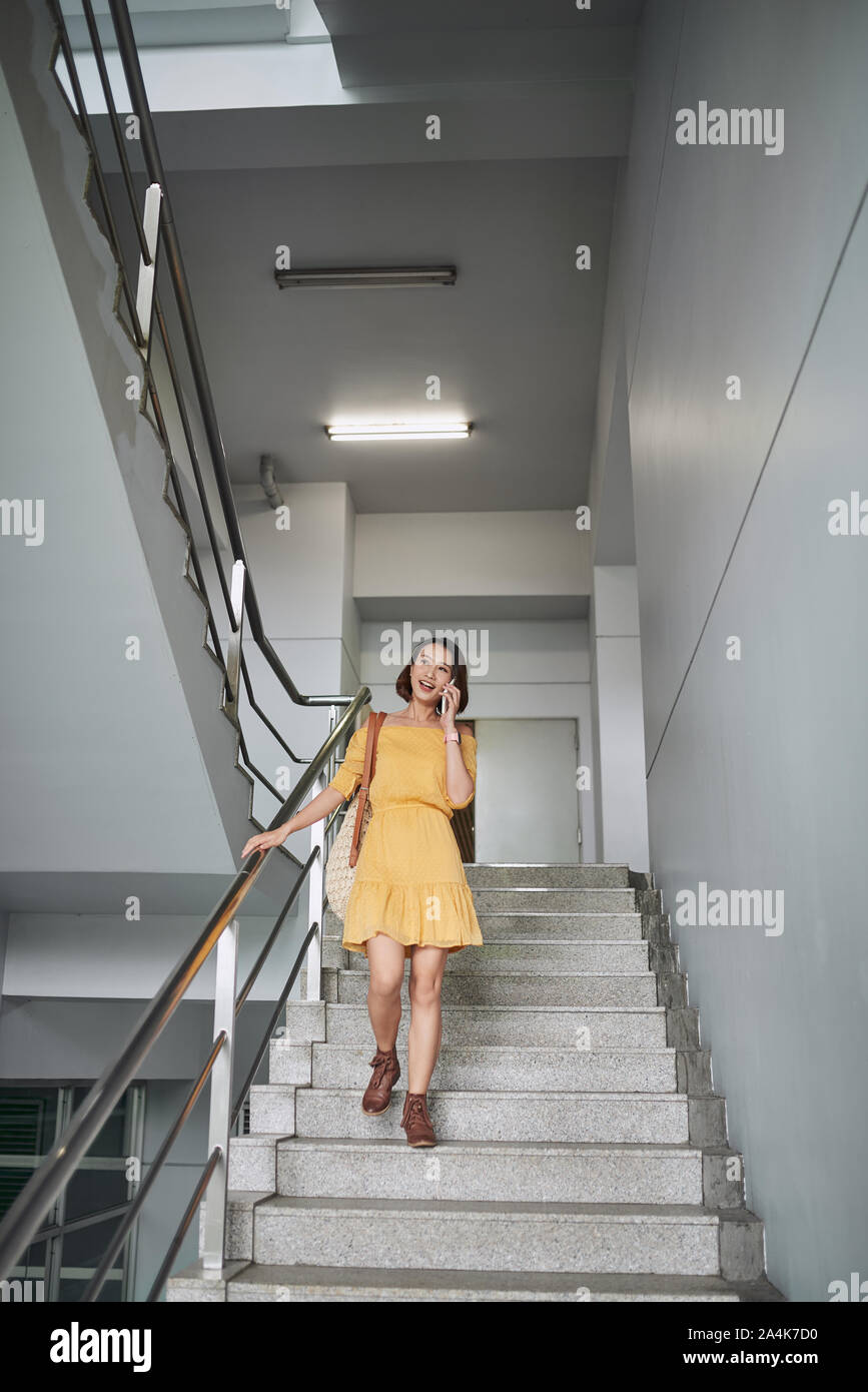 Happy young woman walking downstairs, talking on mobile phone Stock ...