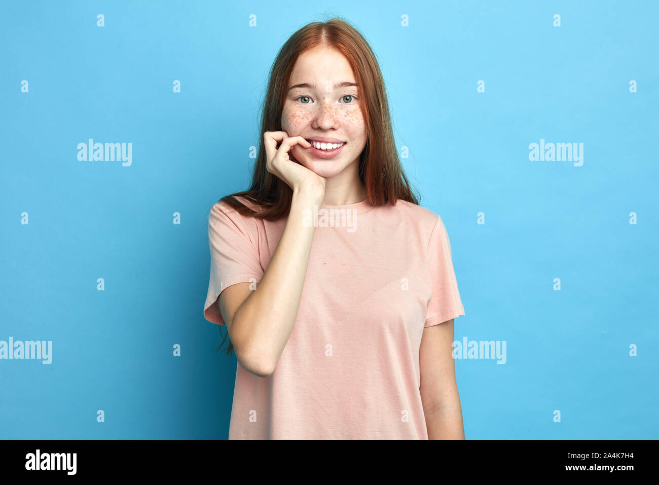 Frightened ginger student with freckled skin looks at camera and bites ...