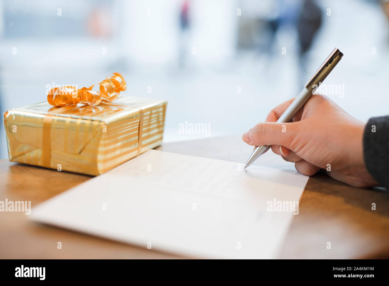Womans hand writing a letter in a cafe, wrapped gift lying beside Stock ...