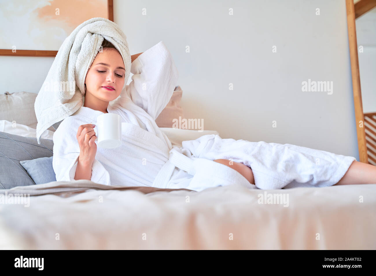 Image of happy woman in white bathrobe with mug of tea in her hands ...