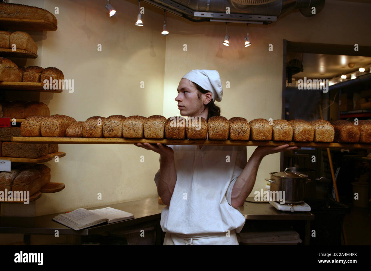 Young man taking a row of bread out of the oven Stock Photo - Alamy
