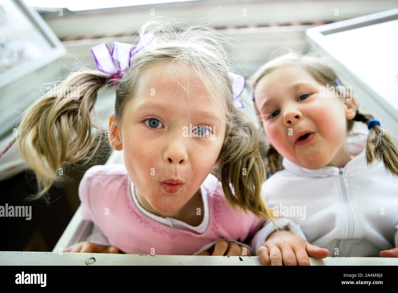 Girls leaning out window making faces Stock Photo - Alamy