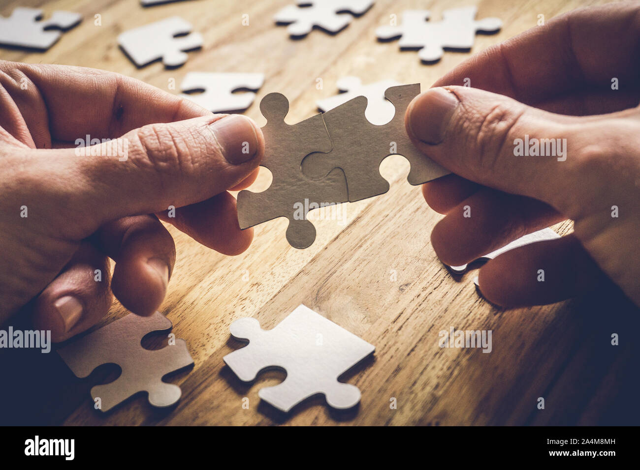 Two hands connect two pieces of the puzzle on a wooden table with many ...
