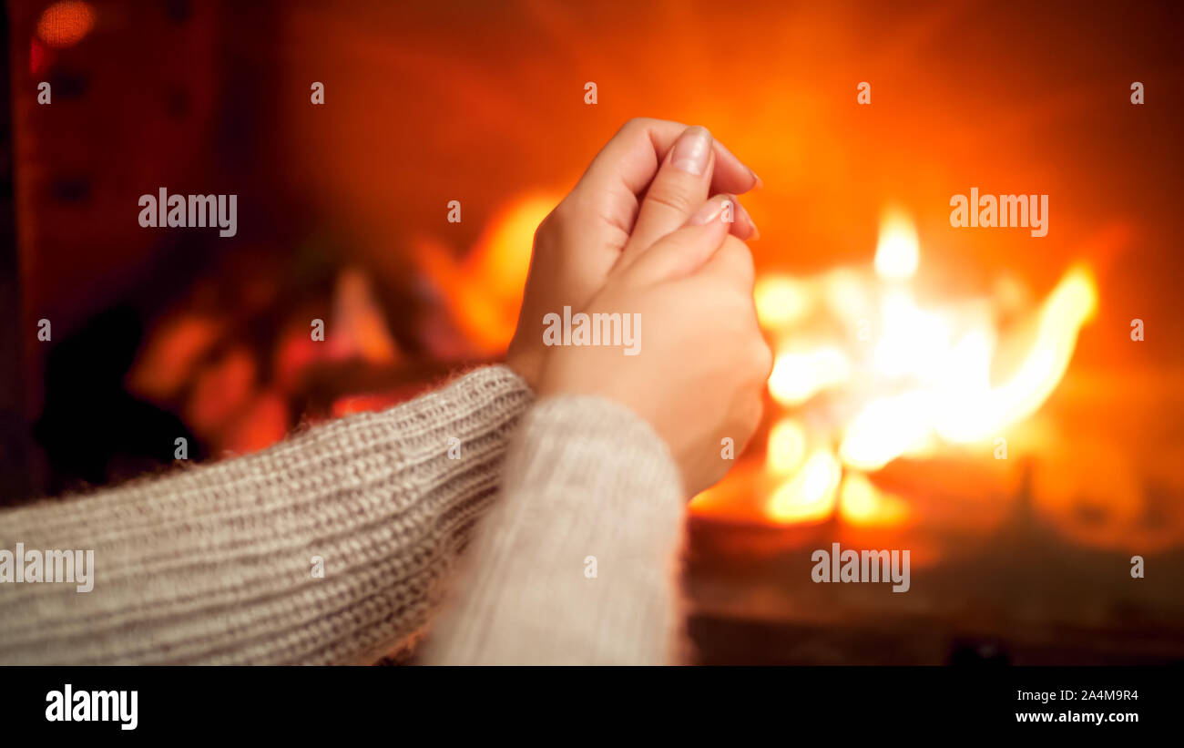 Closeup photo of young wooman feeling cold sitting by the burning fire ...