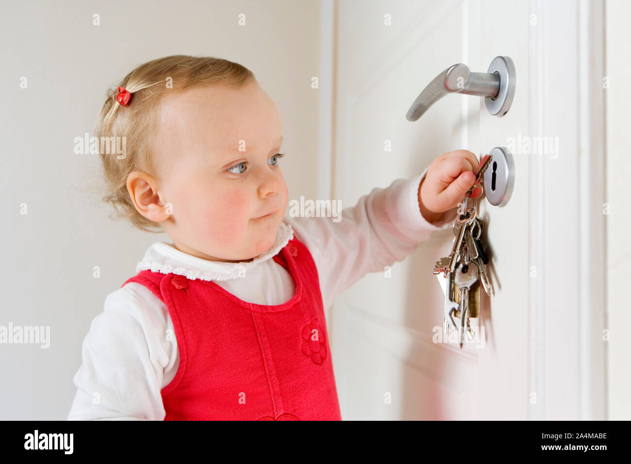 Little girl trying to put the keys in the keyhole to open the door ...