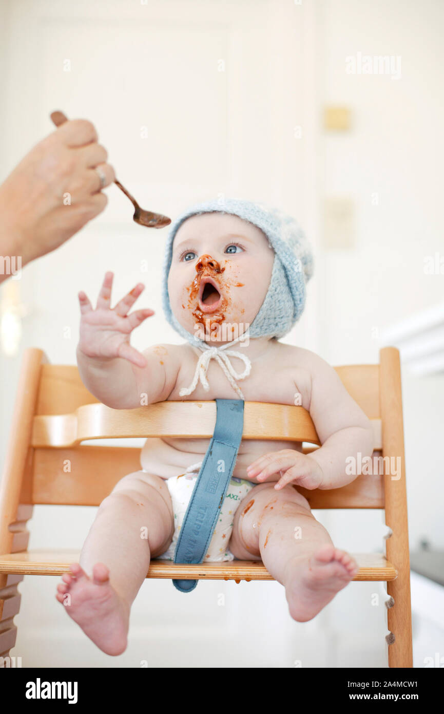 Feeding hungry baby in baby chair Stock Photo - Alamy