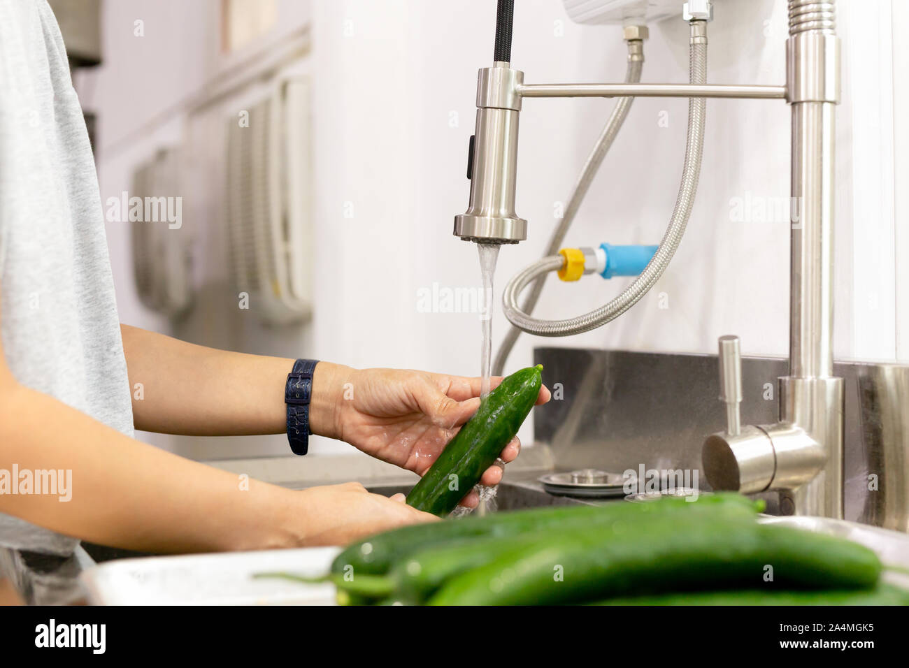 Woman washing cucumbers in running water in kitchen sink Stock Photo ...