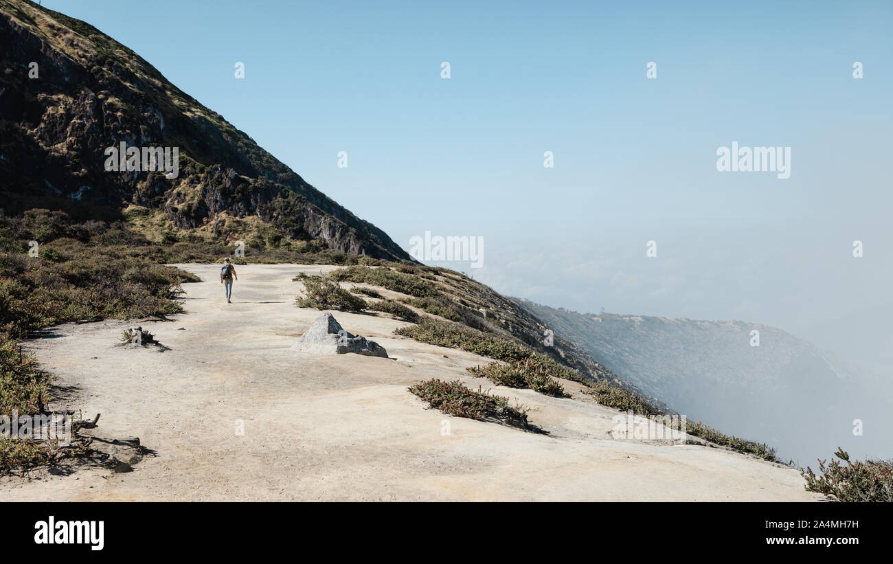 Young woman walking around Kawah Ijen volcano crater with acid lake ...