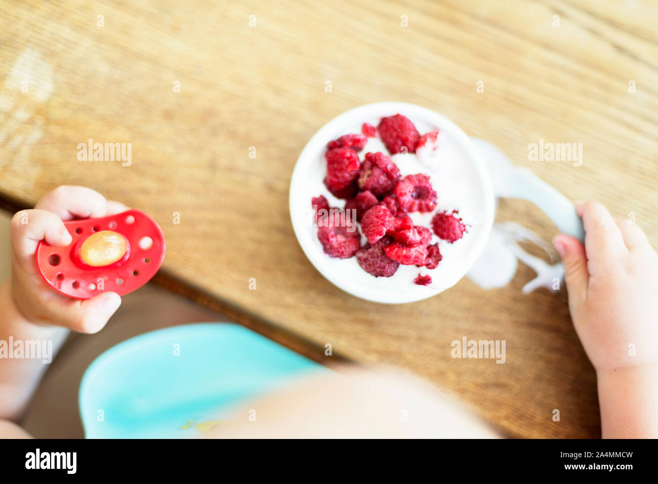 Baby holding pacifier, yogurt with raspberries on table Stock Photo - Alamy