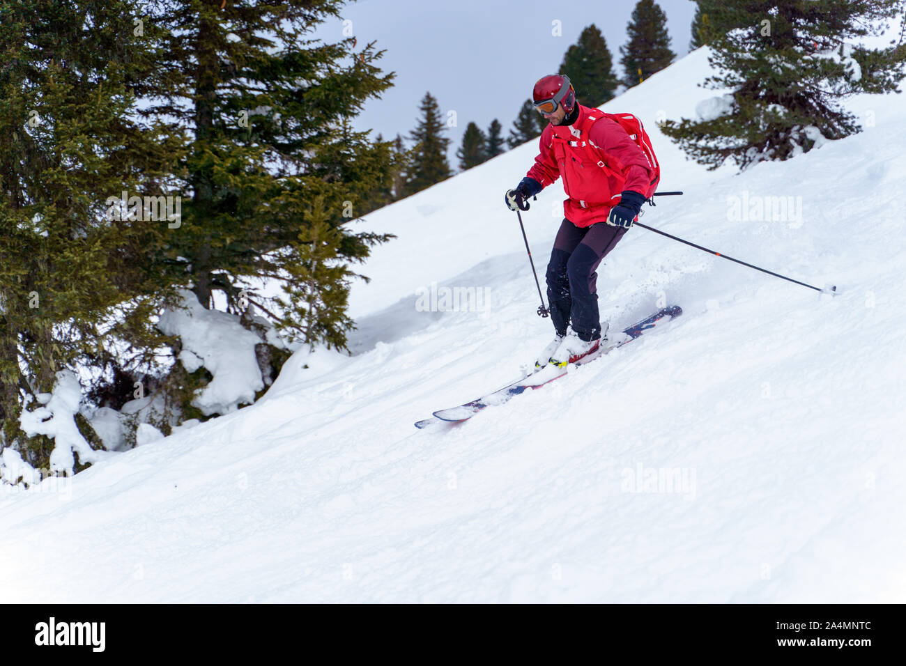 Side photo of sports man in red jacket and with backpack skiing in ...