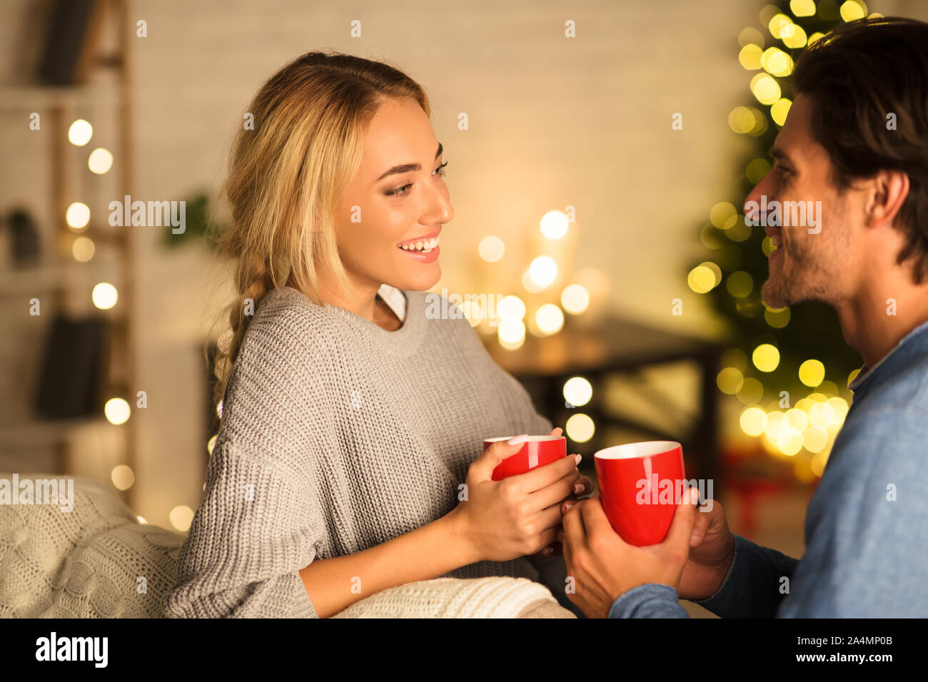 Loving couple drinking tea in front of Christmas tree Stock Photo - Alamy