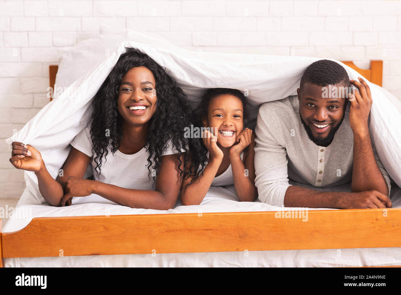 Cheerful black family of three hiding under blanket on bed Stock Photo ...