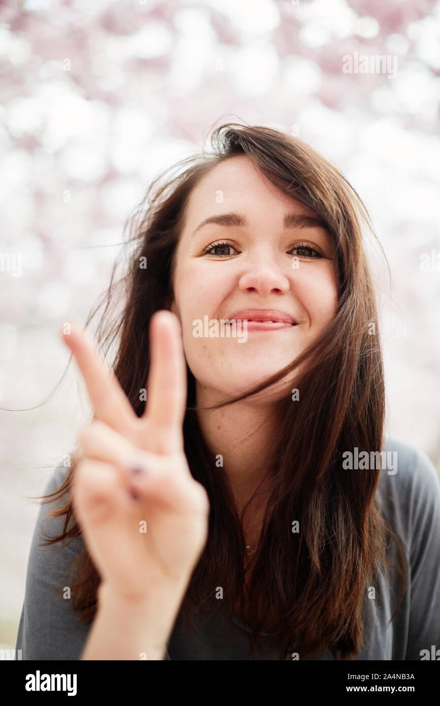 Young woman making peace sign Stock Photo - Alamy