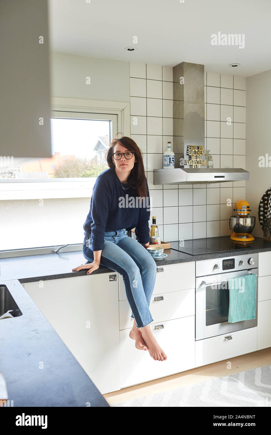 Young woman sitting on kitchen counter Stock Photo - Alamy