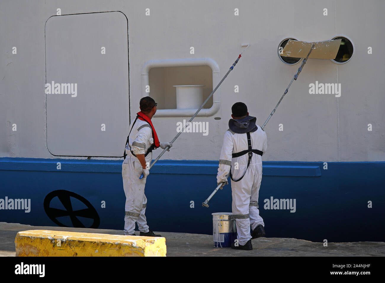 Two crew members doing maintenance work painting the outside of a ship ...