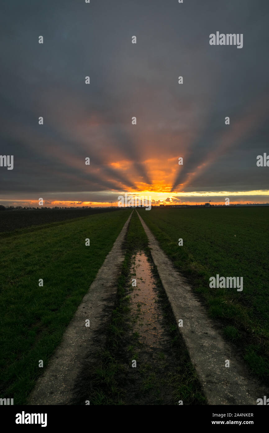Sun rays shine at the base of the clouds after sunset. A path is ...
