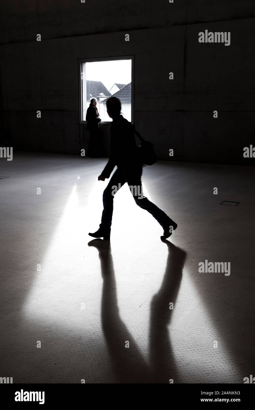 Light falls through a square window into a large, empty room, person ...