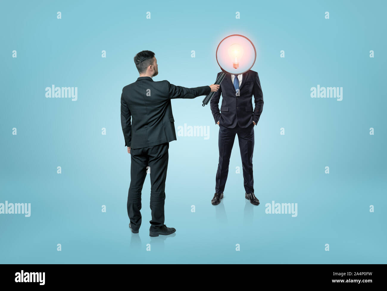 Businessman directing magnifying glass on lamp-headed man Stock Photo ...