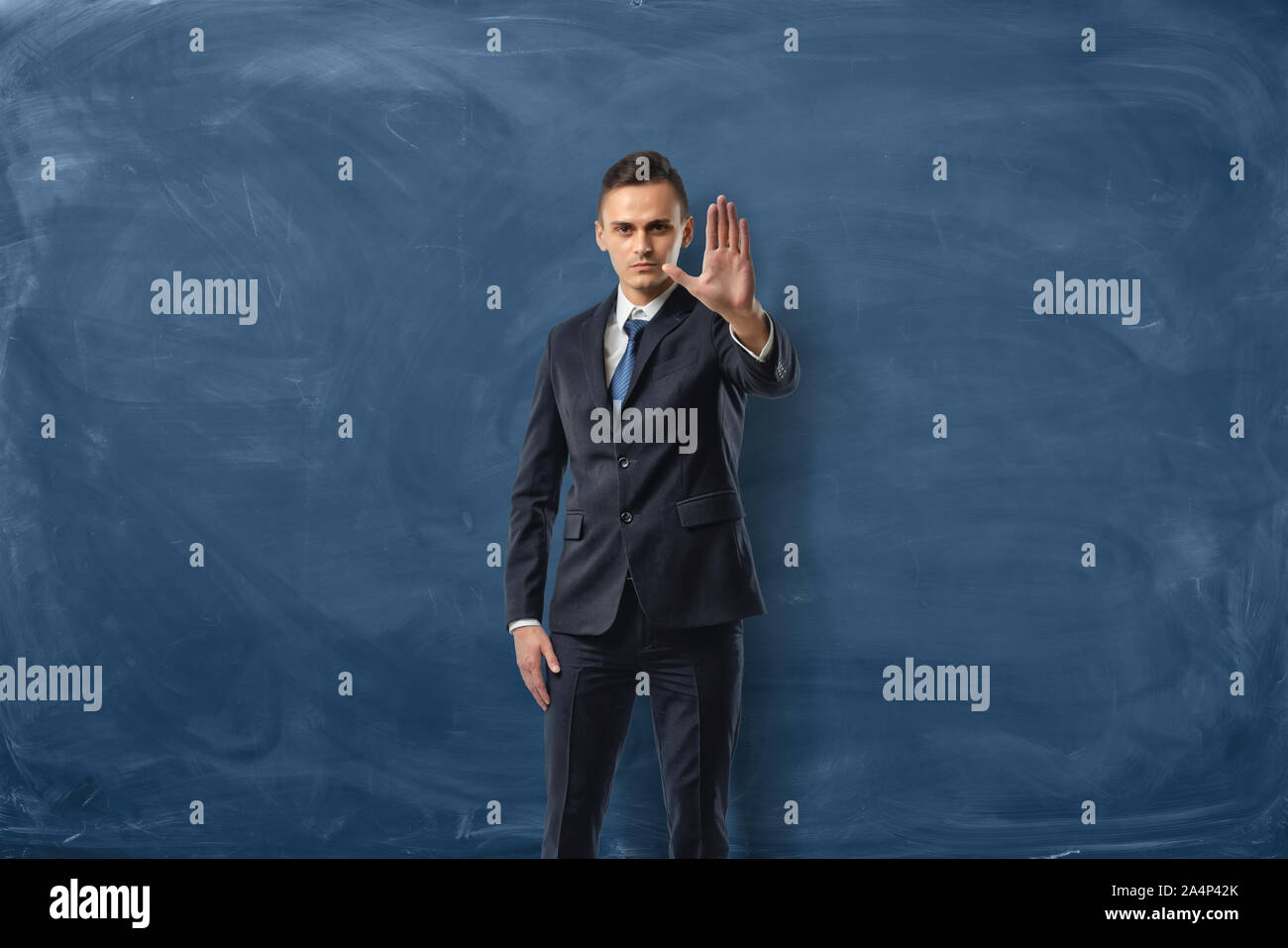 Businessman on blue chalkboard background holding one hand in a stop ...