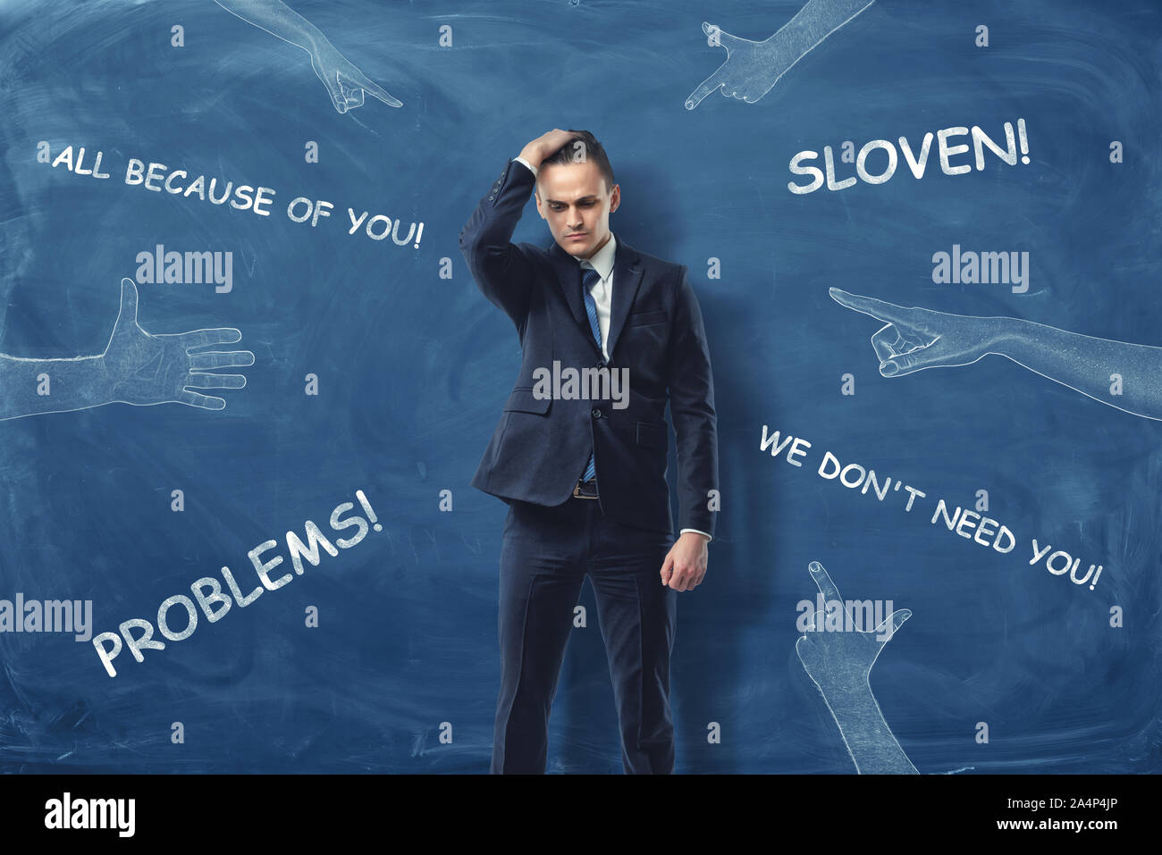 Embarrassed businessman standing near dark blue wall with hands ...