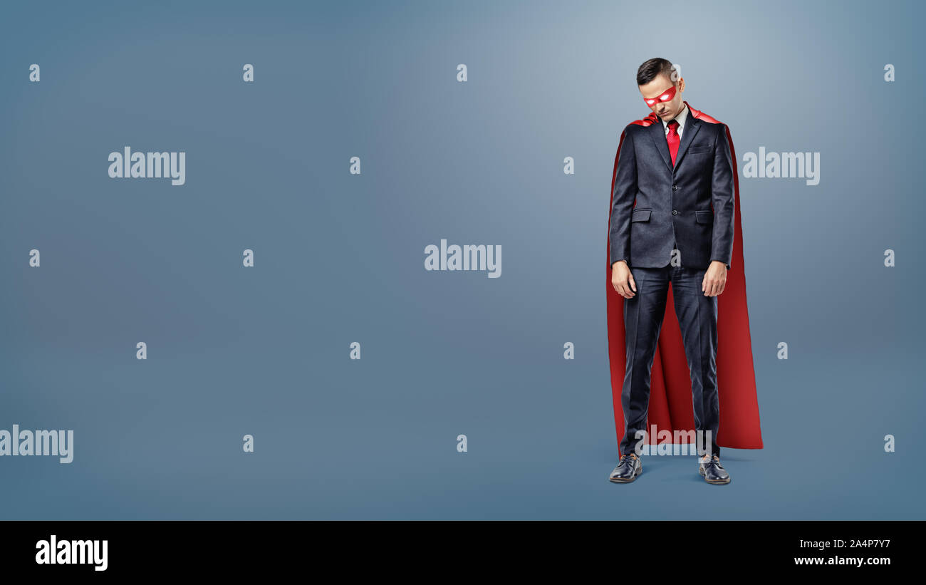 A sad businessman in a superhero red cape standing on dark blue ...