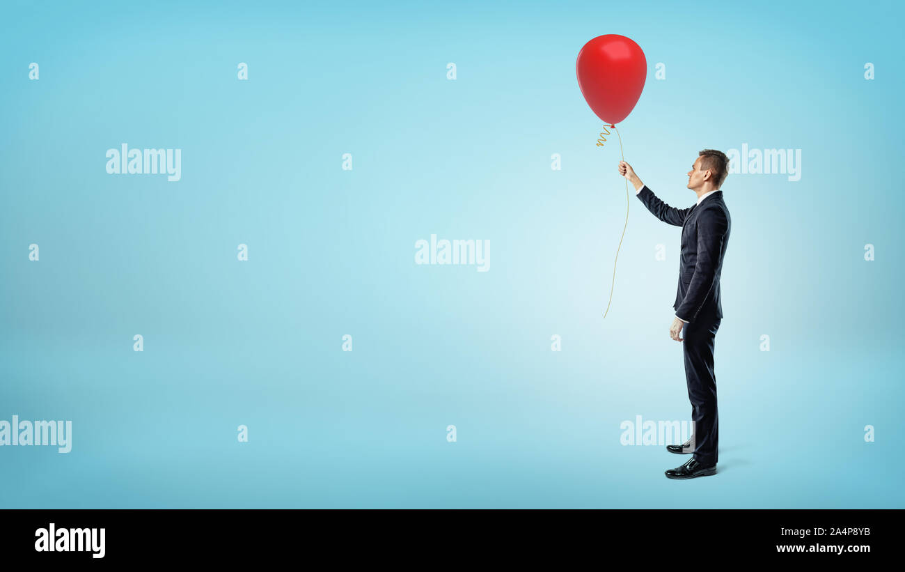 A businessman standing in side view on blue background and holding a ...