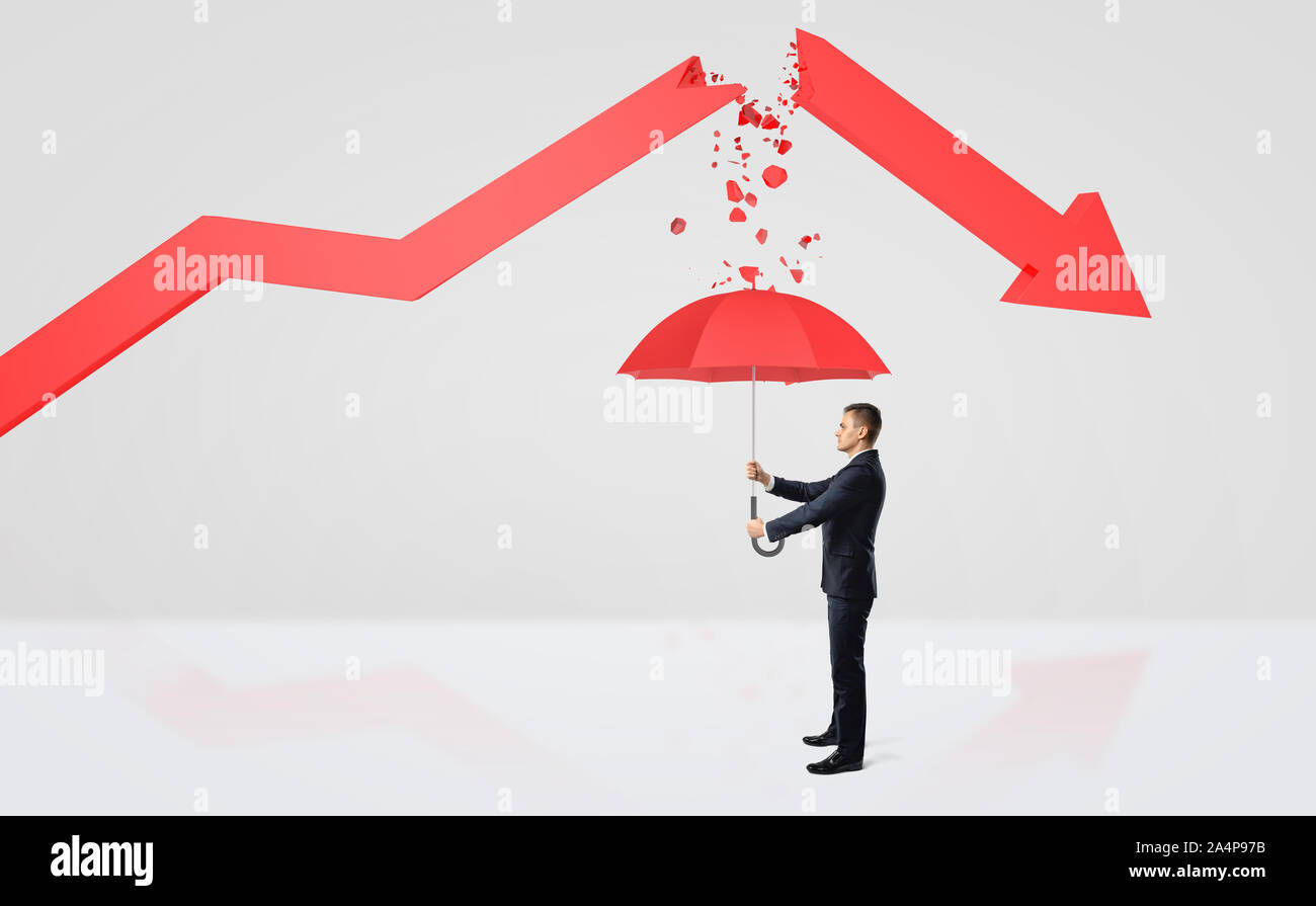 A tiny businessman hiding under a red umbrella from the rubble of a ...