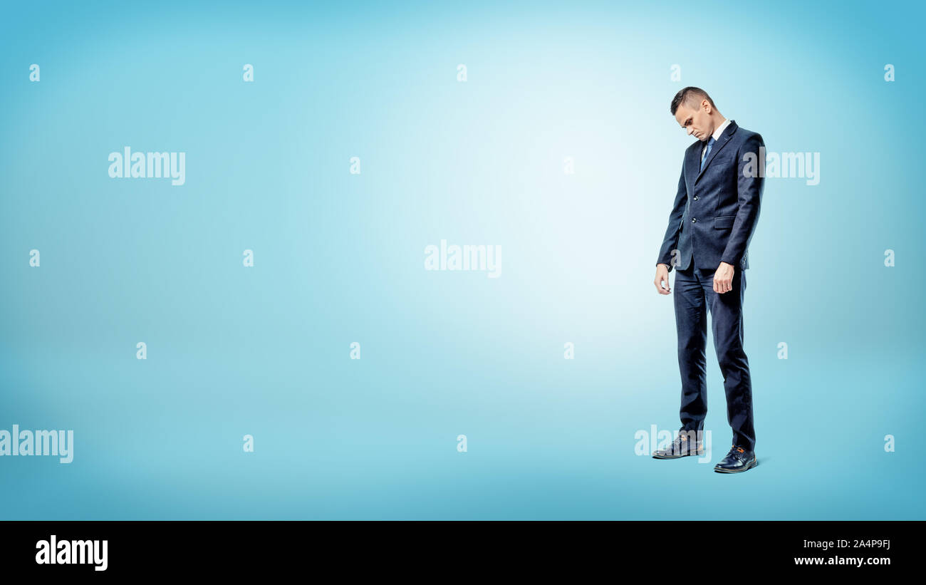A sad businessman standing on blue background looking down with slumped ...