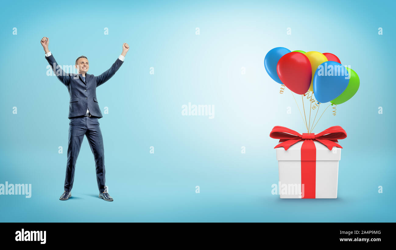 A happy businessman with hands raised up standing behind a gift box ...