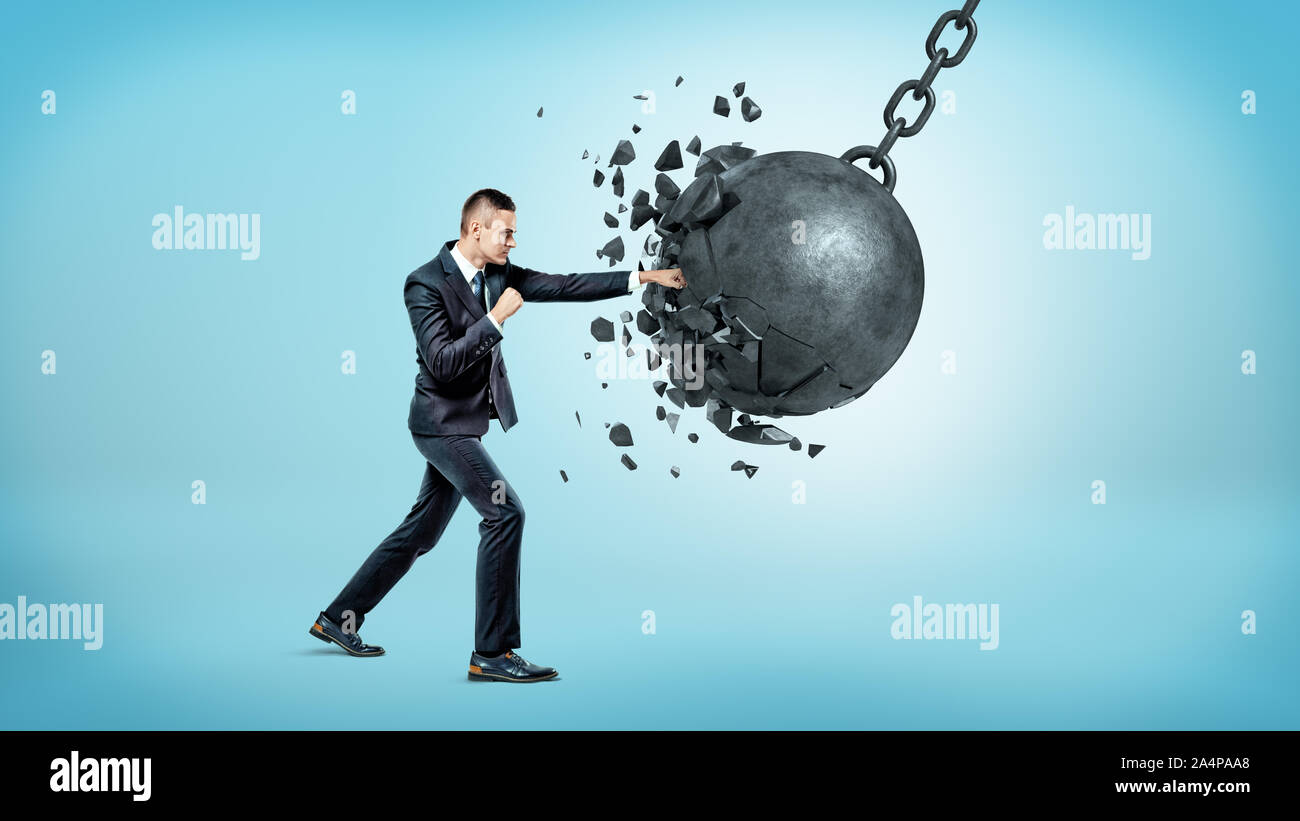 A businessman in full height punching and breaking a huge wrecking ball ...
