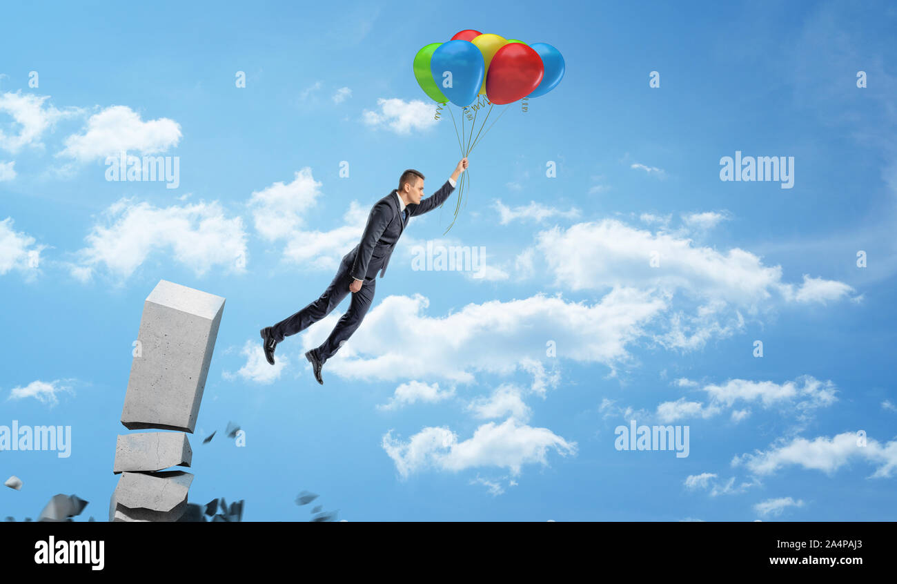 A businessman holding a set of colorful balloons on a string and flying ...