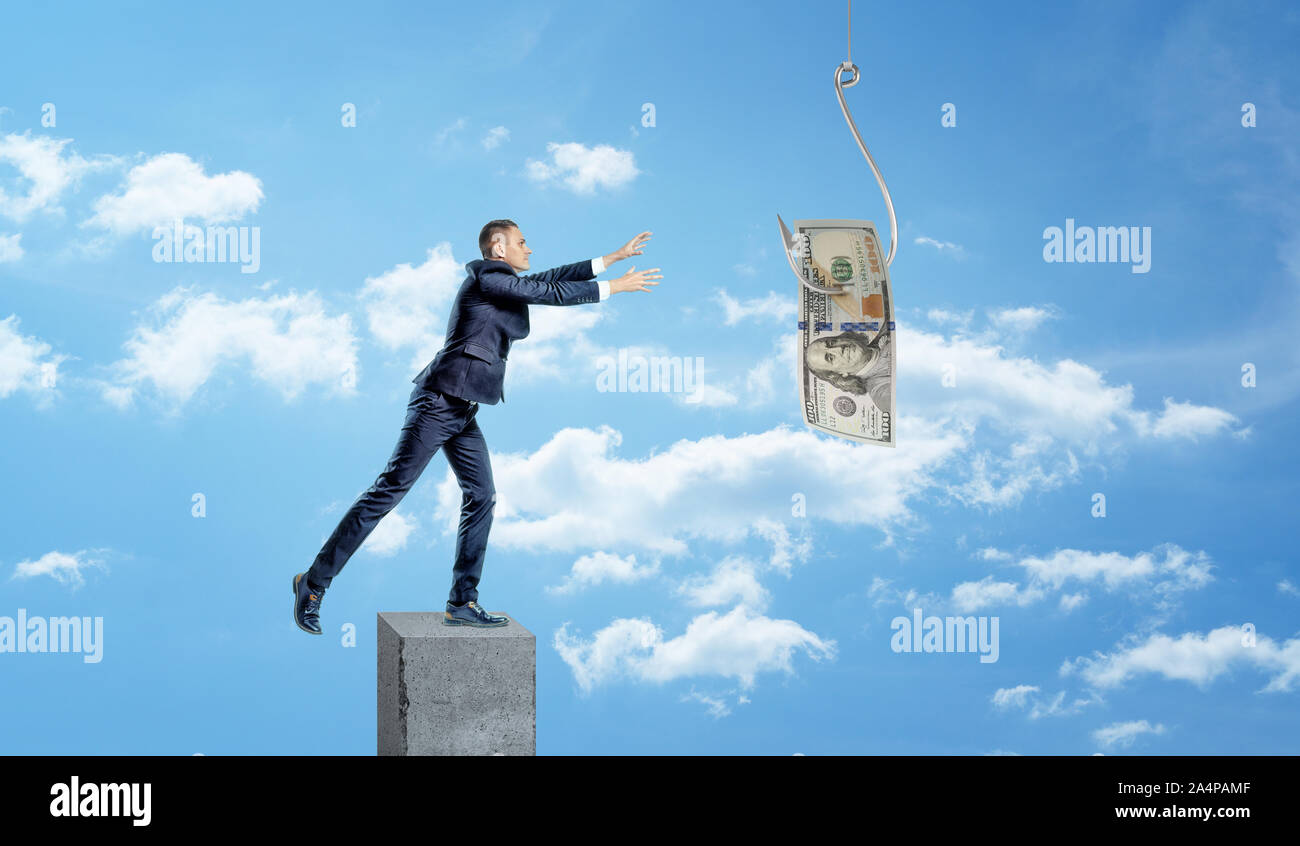 A small businessman standing on a concrete column and catching a dollar ...