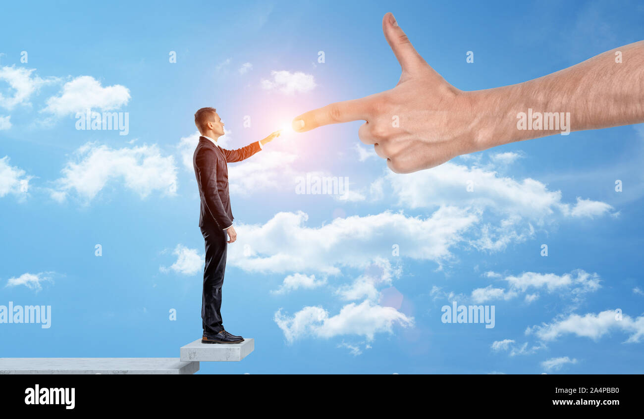 A businessman standing among the clouds to touch fingers with a giant ...