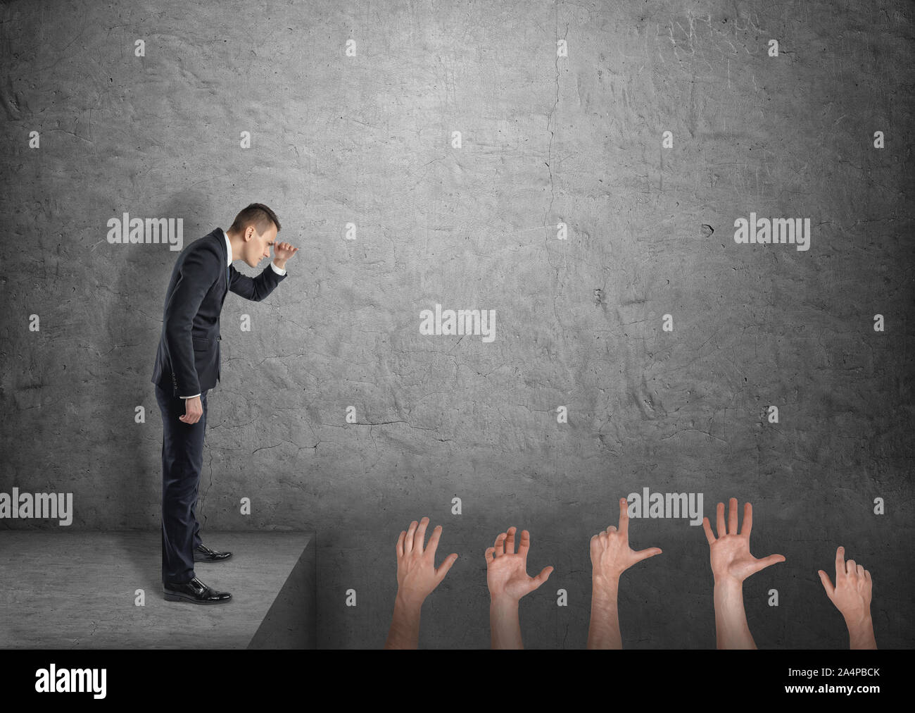 A businessman on grey concrete background looks down into an abyss full ...