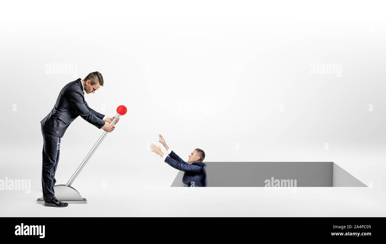 A businessman turns a large lever helping another man fallen inside a ...