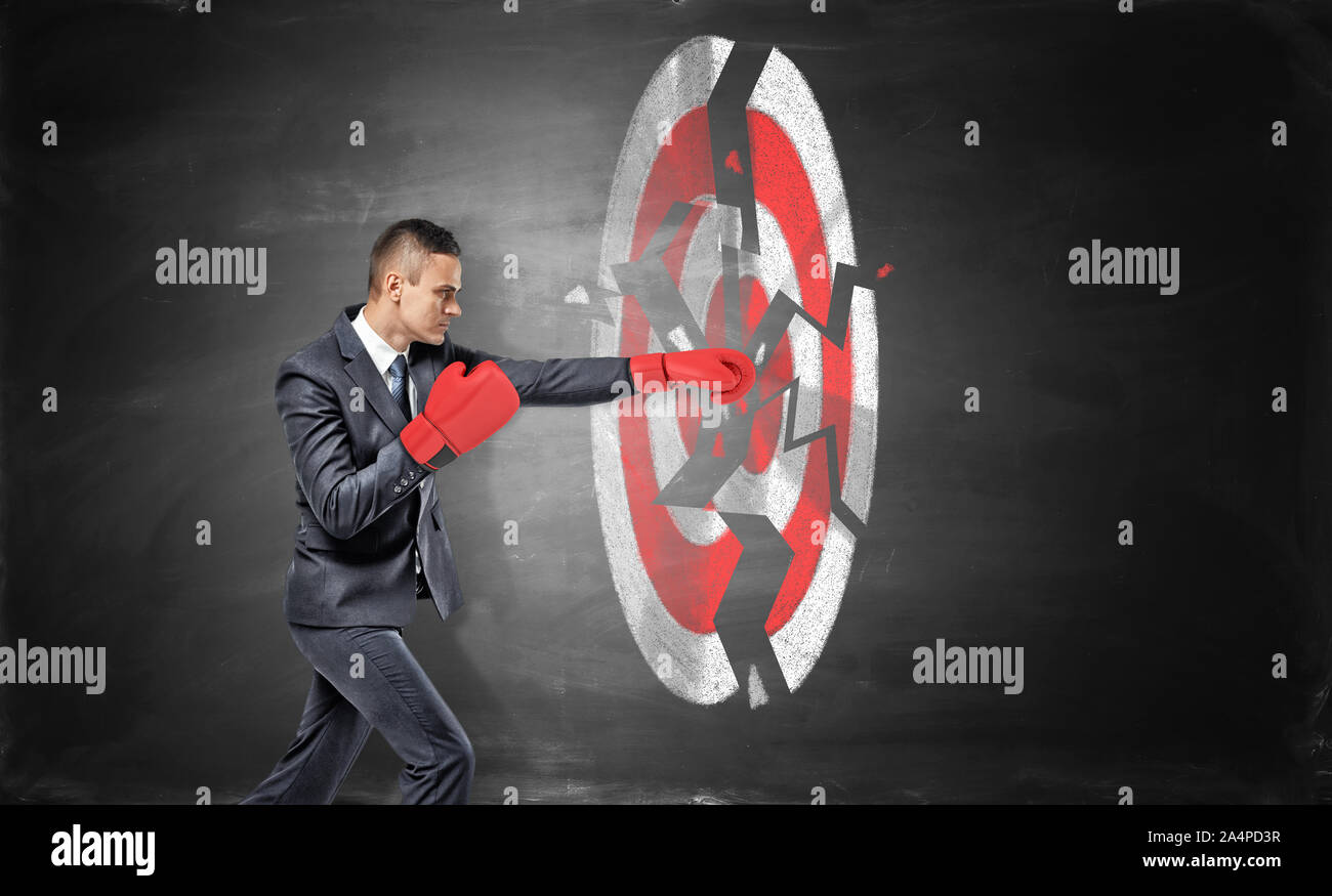 A businessman wears boxing gloves and breaks a chalk drawing of a round ...